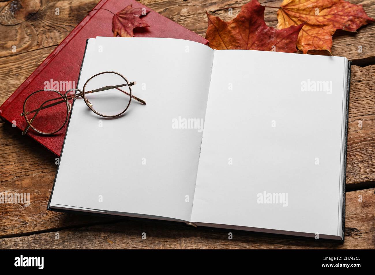 Opened book with blank pages, eyeglasses and autumn leaves on wooden ...