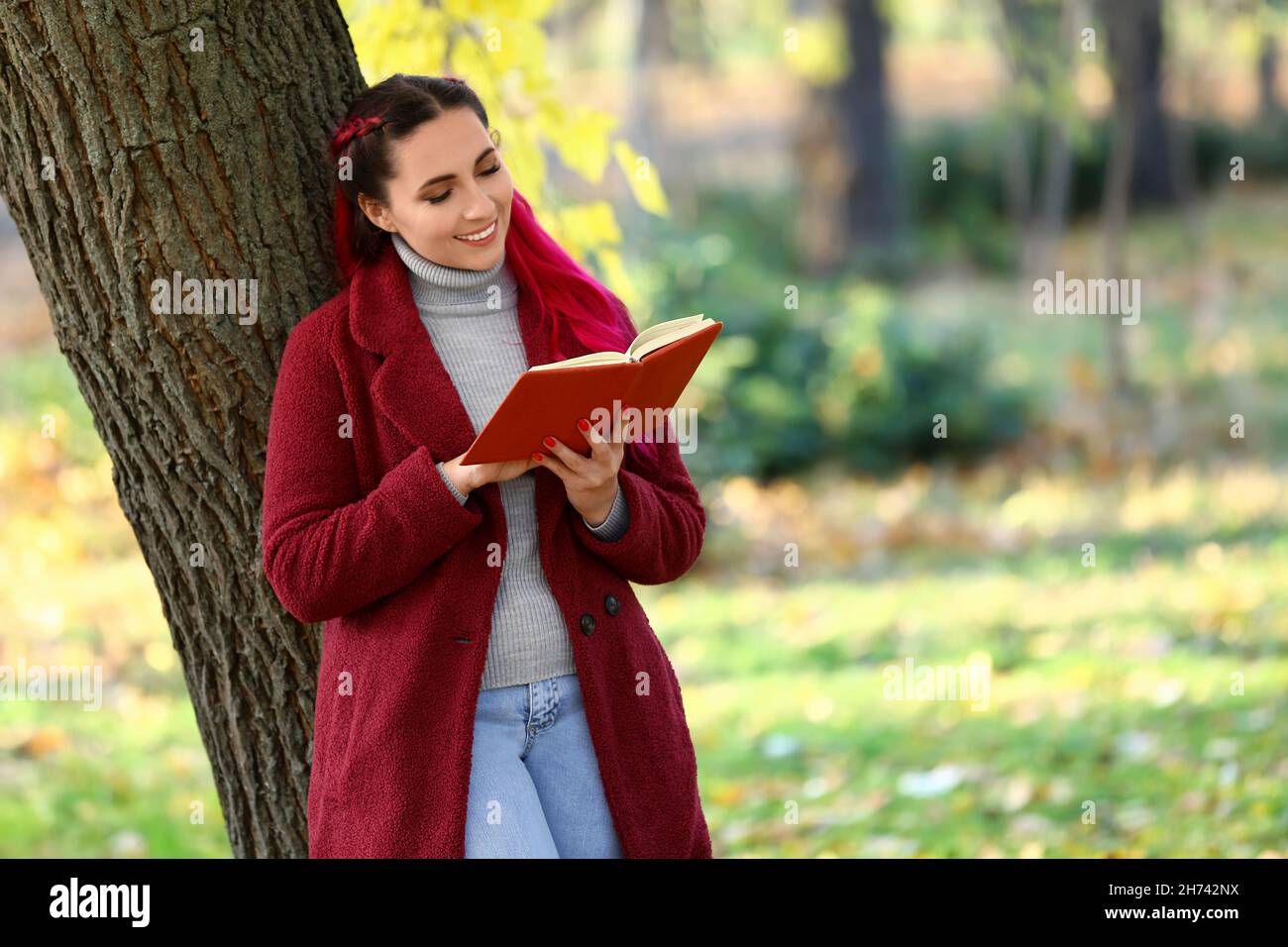 Beautiful woman reading book near tree in autumn park Stock Photo - Alamy