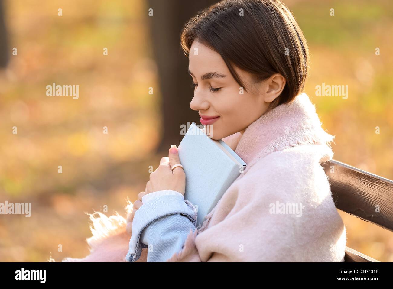 Young woman with plaid sitting on bench and hugging book Stock Photo ...