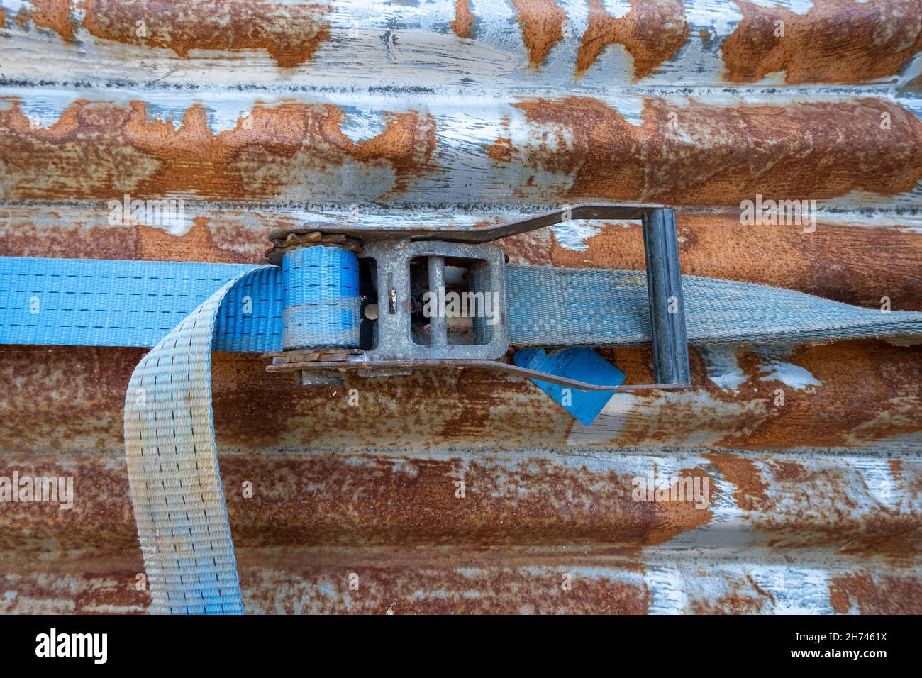 A blue rachet strap wrapped around a rusty corrugated iron metal sheet ...