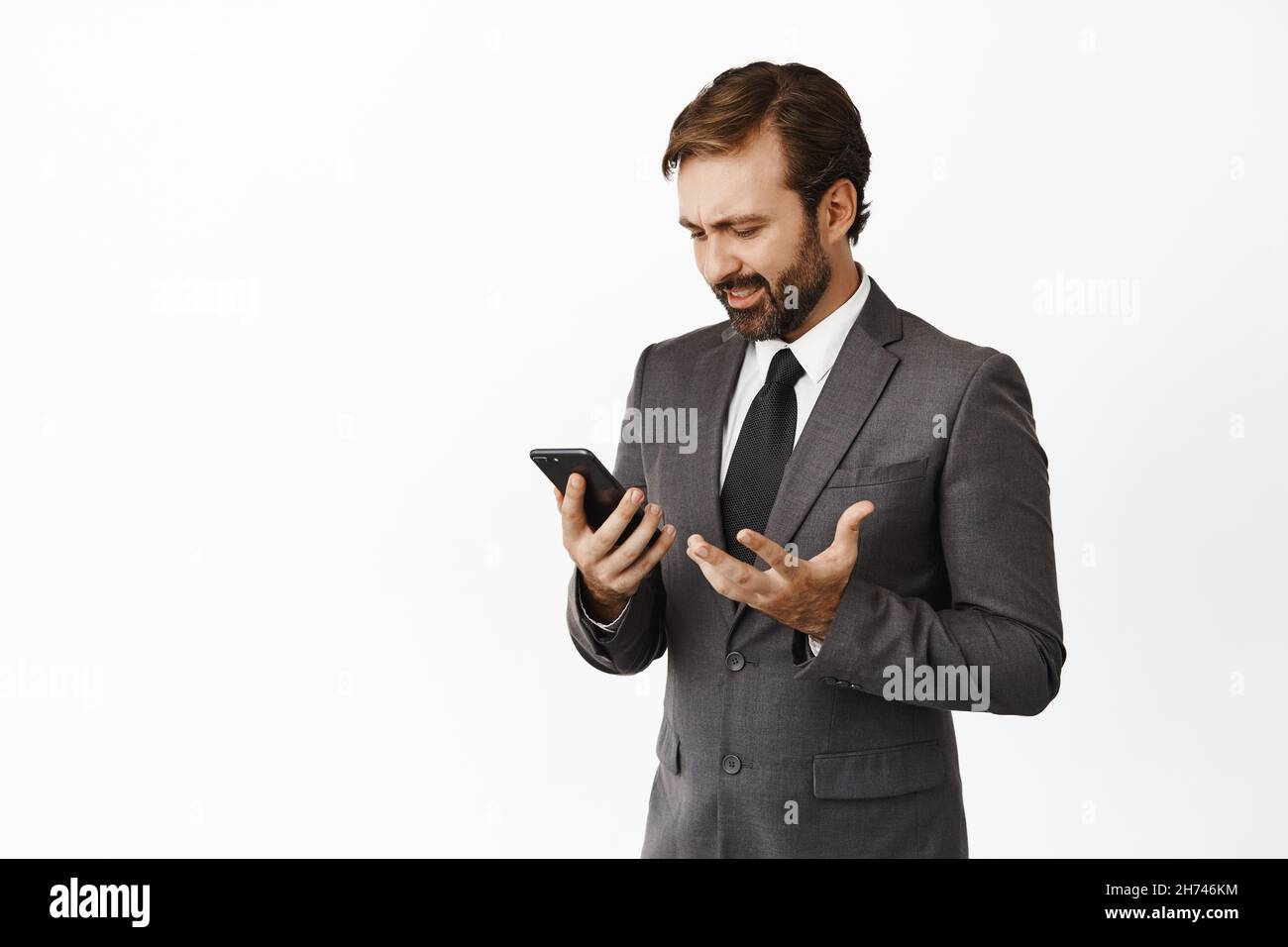 Confused businessman looking at his mobile phone screen, having problem ...