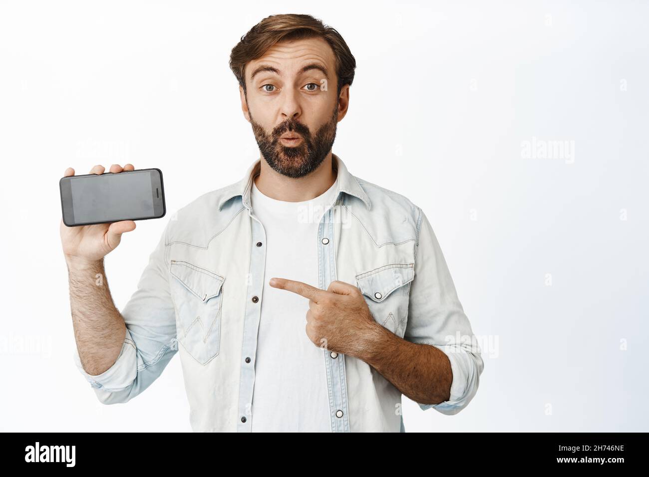 Excited guy pointing at horizontal smartphone screen and looking amazed ...