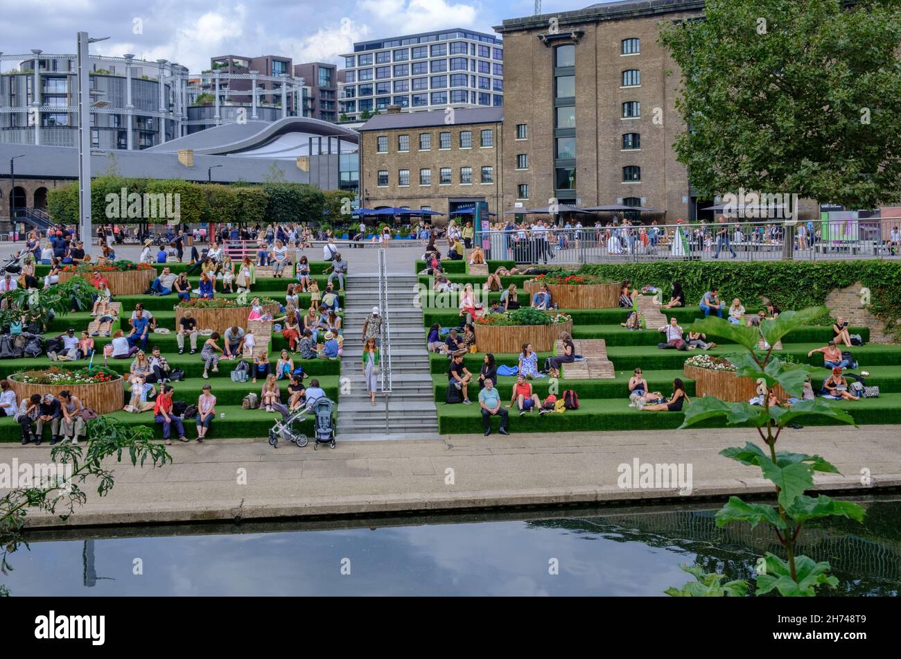 People relax on wide green steps next to Regent's Canal at Granary ...