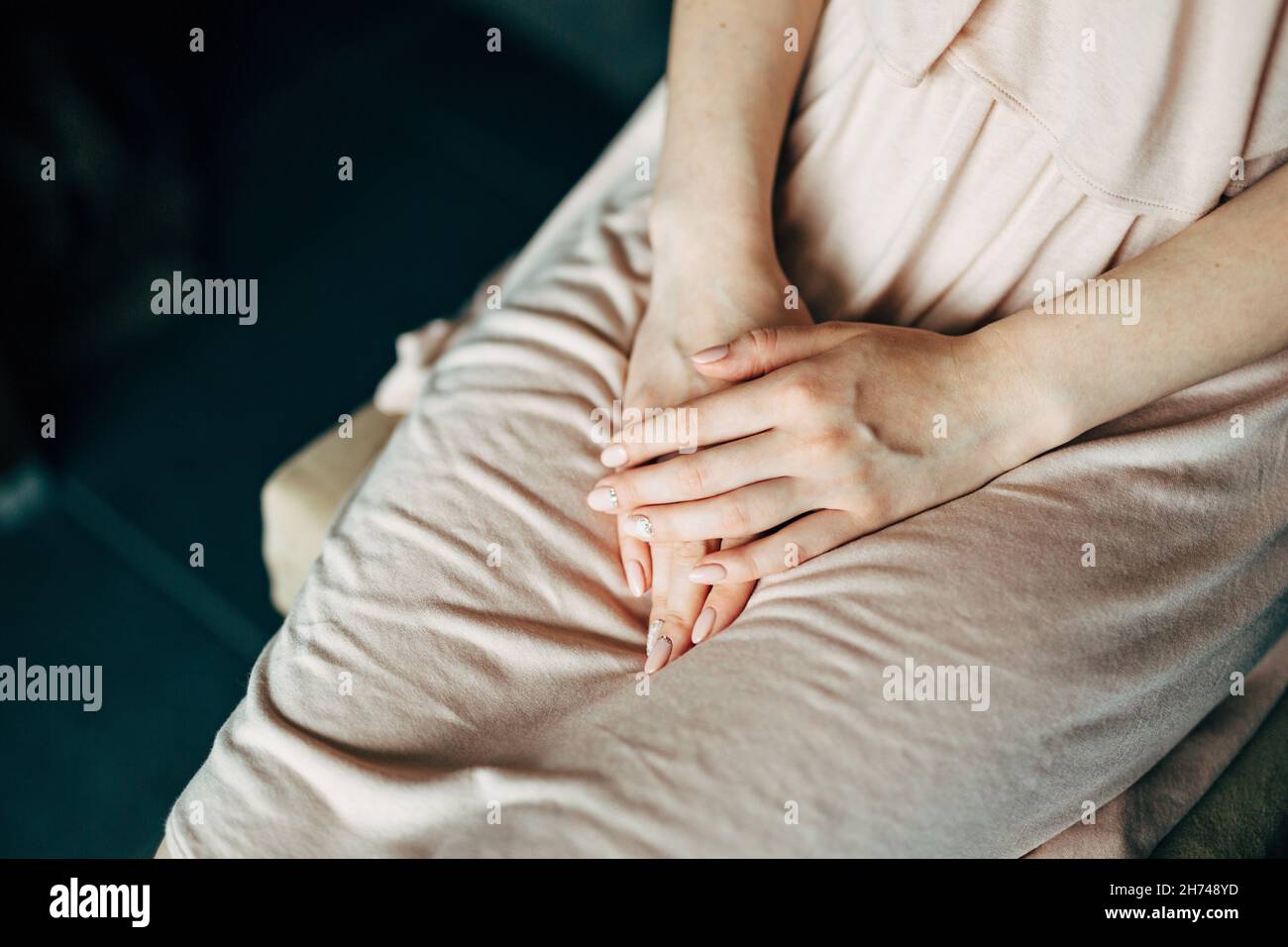Woman in a beige dress folded her hands in her lap, sitting on a chair ...