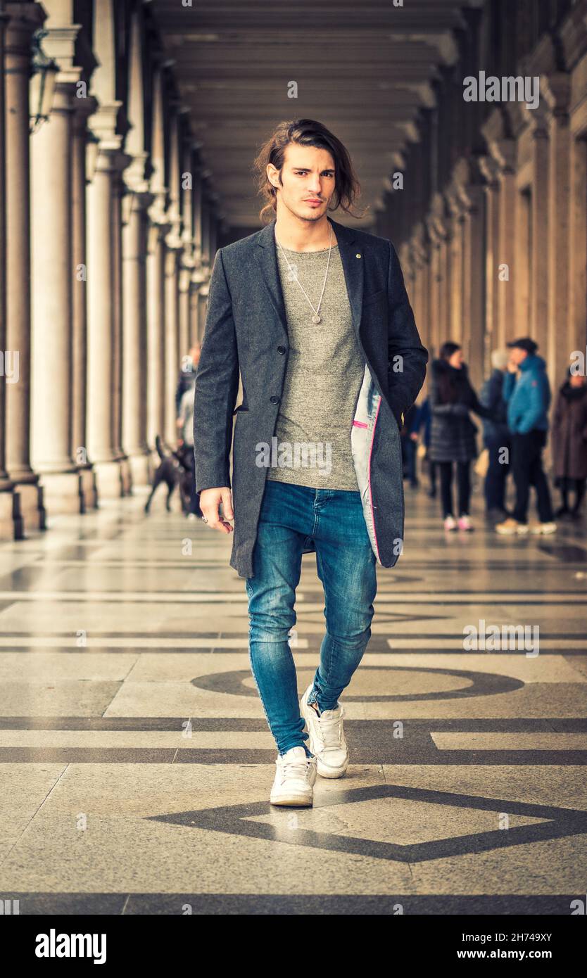 Elegant young man outdoor wearing wool coat and jeans under colonnade ...