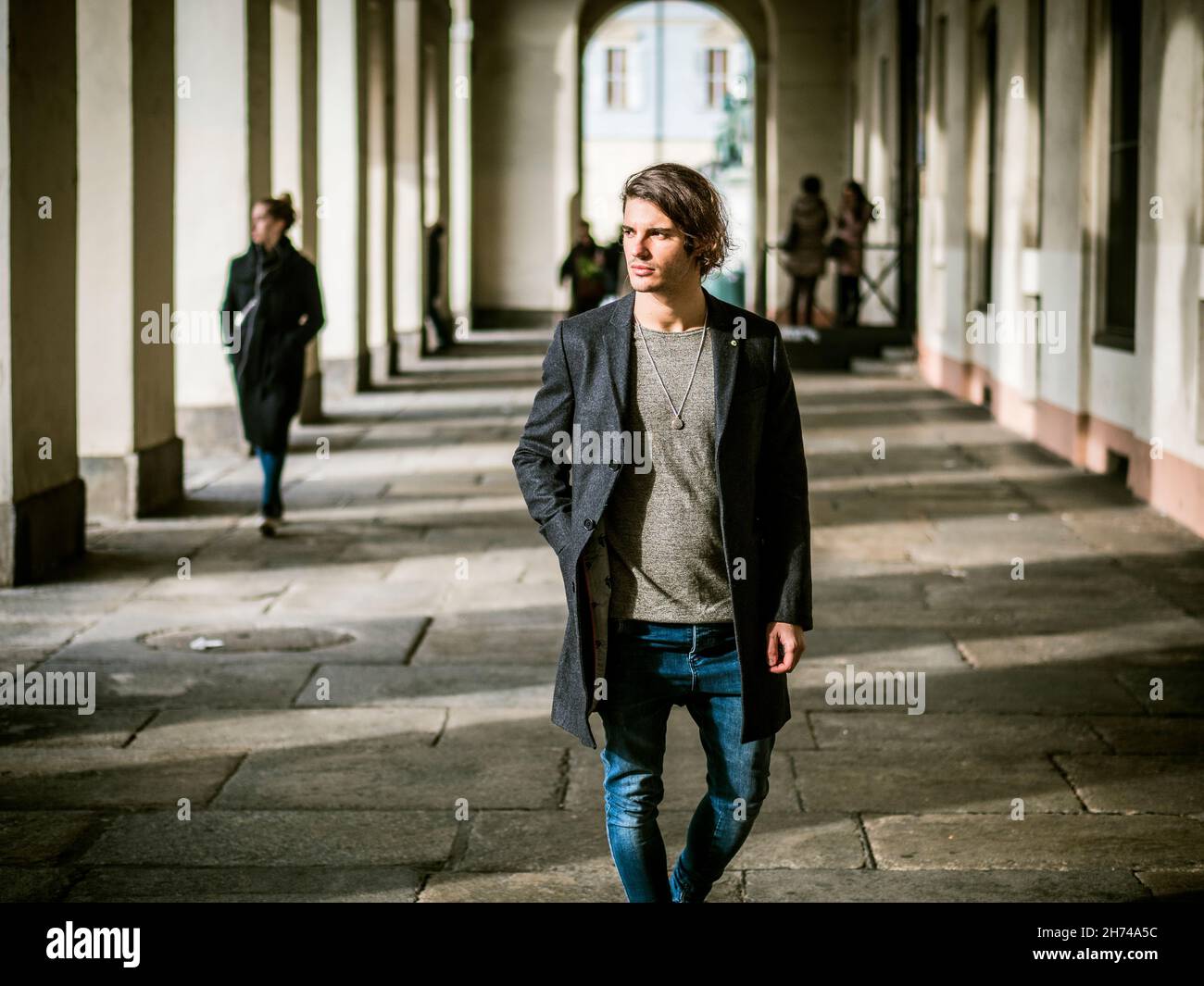 Elegant young man outdoor wearing wool coat and jeans under colonnade ...