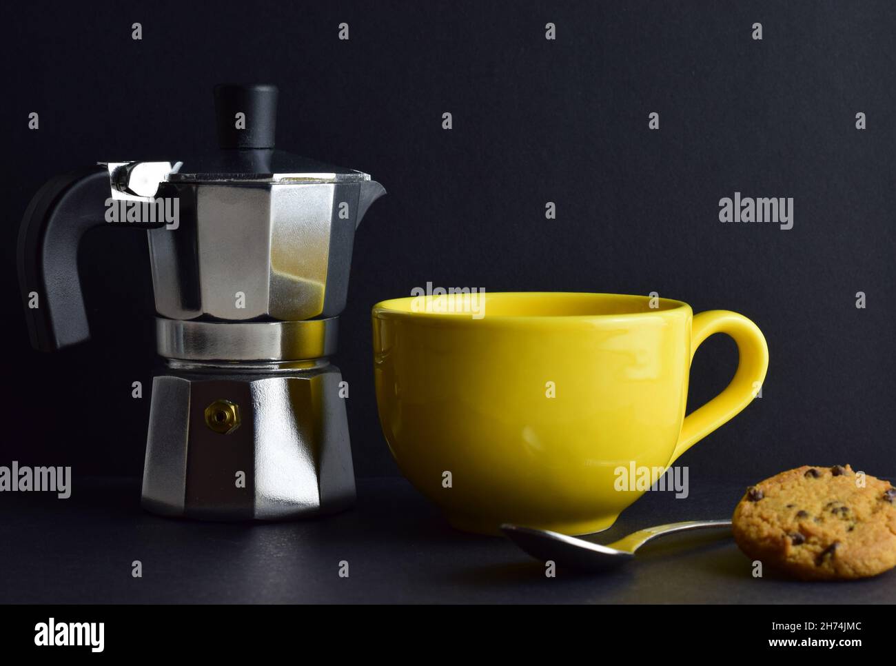 Moka pot, yellow mug, biscuit, and spoon isolated in the black ...
