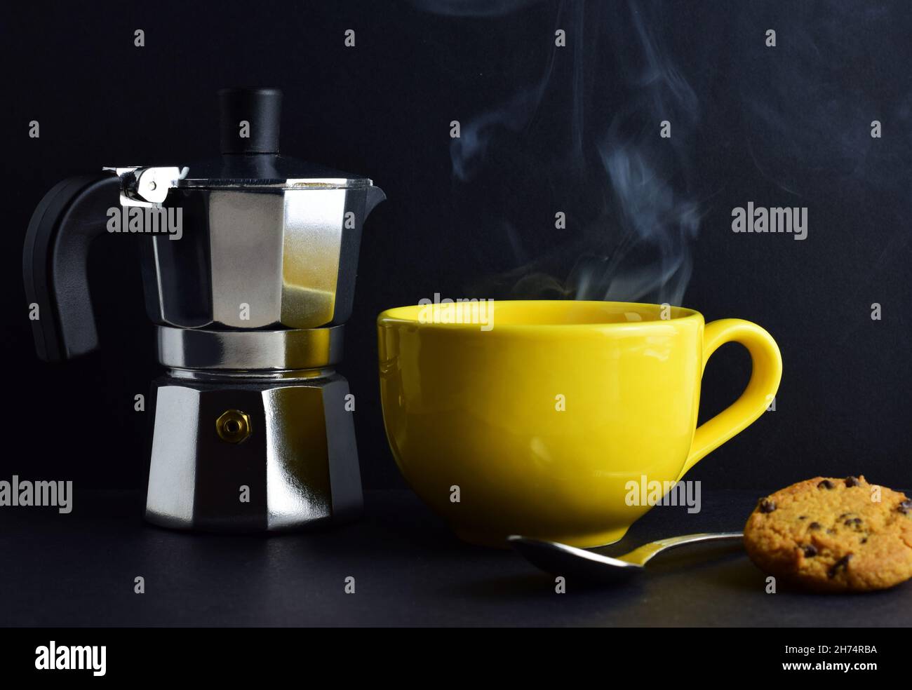 Moka pot, yellow cup with a hot drink, and biscuit in the dark ...