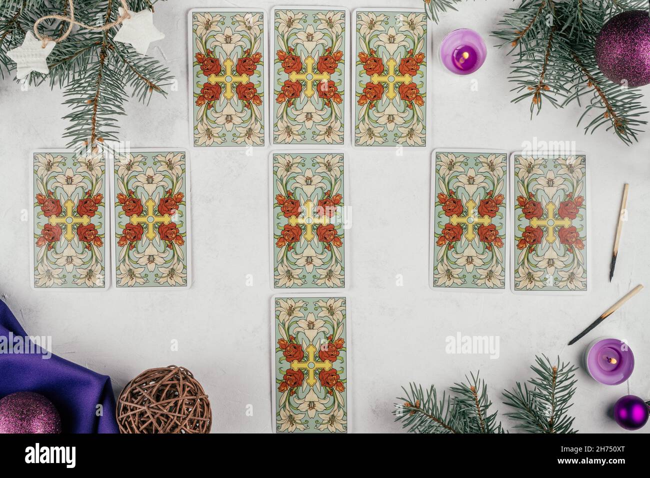 Tarot cards spread on white concrete surface with Christmas tree branches, candles and ...