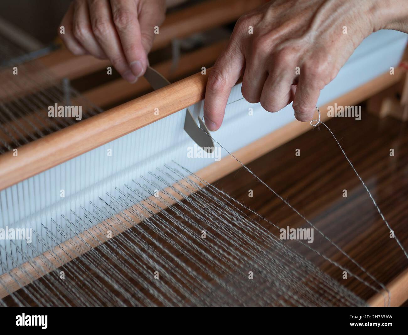 Woman is warping a wooden handloom. Hands holding a heddle hook and ...