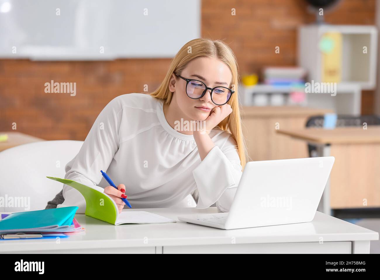 Young female teacher working with laptop at desk in classroom Stock ...