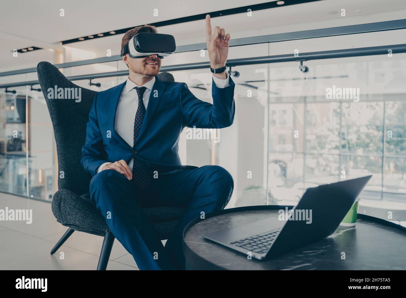 Well-groomed CEO man in formal suit wearing VR headset goggles, while ...