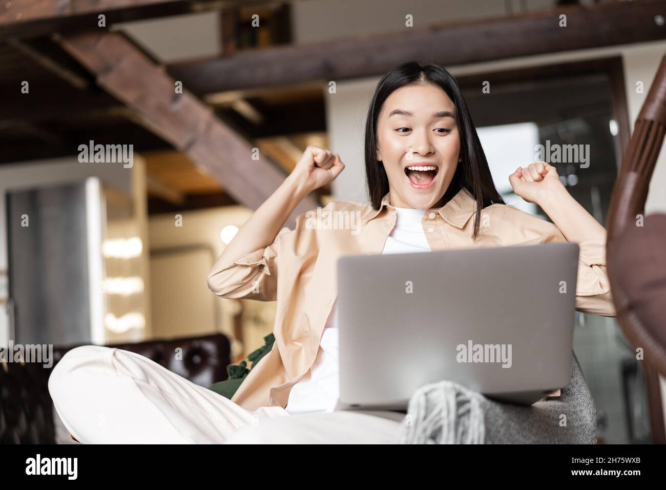 Excited asian woman triumphing, celebrating victory, looking at laptop ...