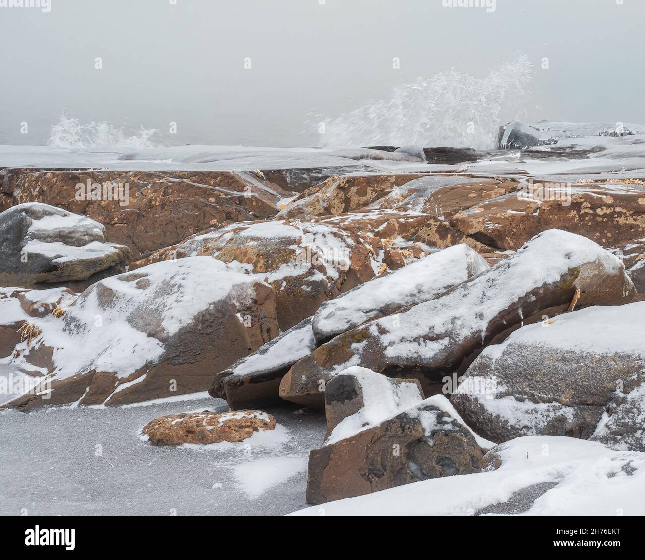 Winter shoreline with icy waves splashing over large rocks and freezing ...