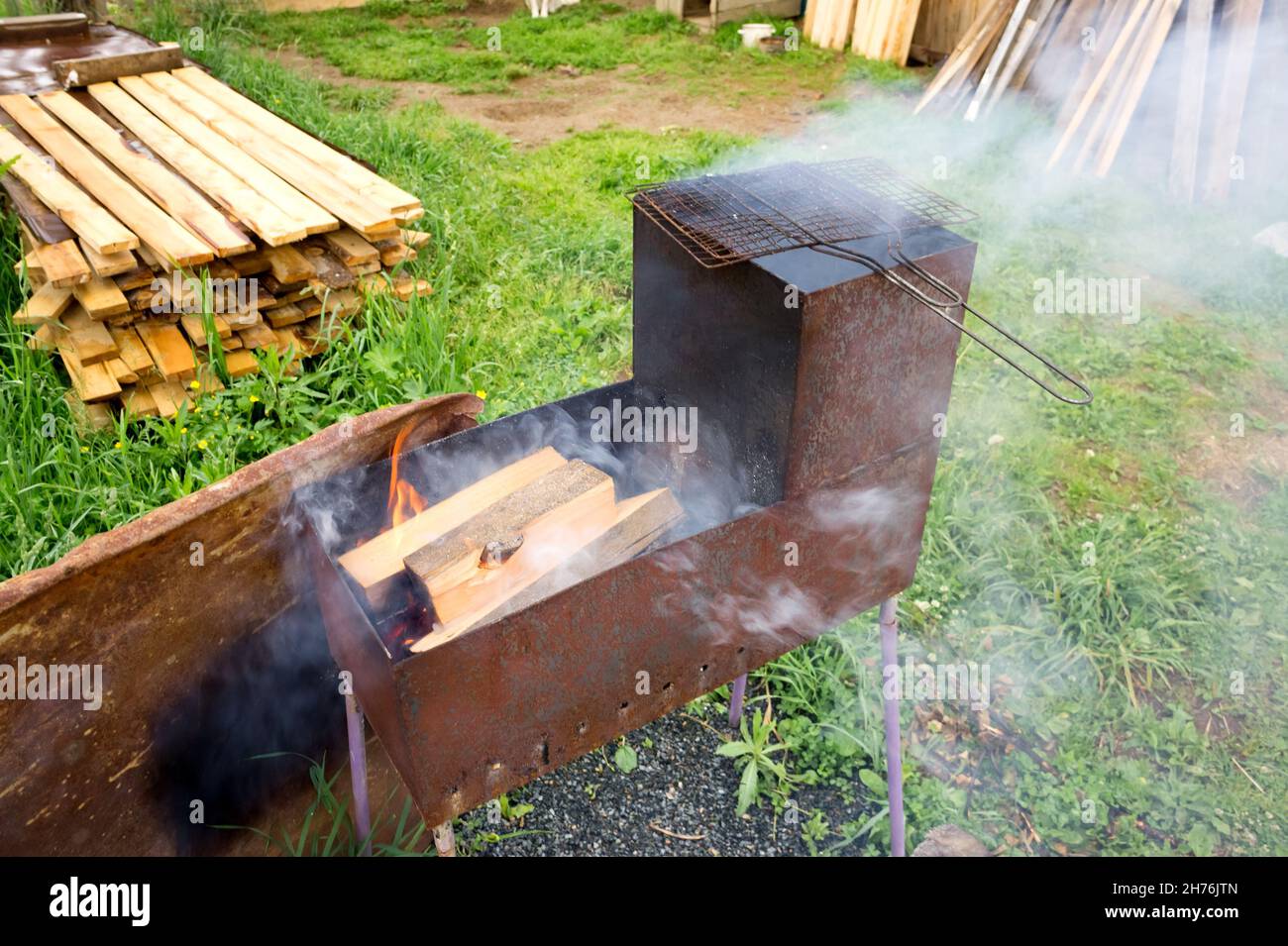 Firewood is lit in a homemade iron barbecue on the lawn on a summer day ...
