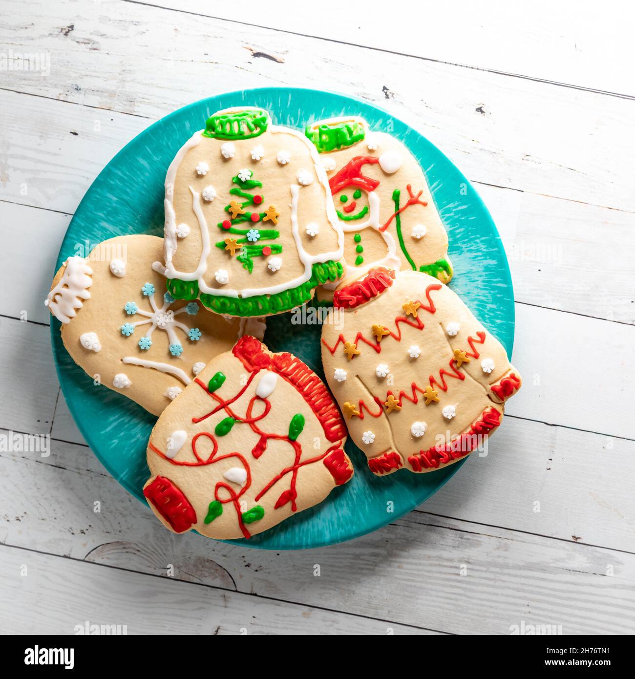 A plate full of colourful ugly Christmas sweater cookies on a wooden ...