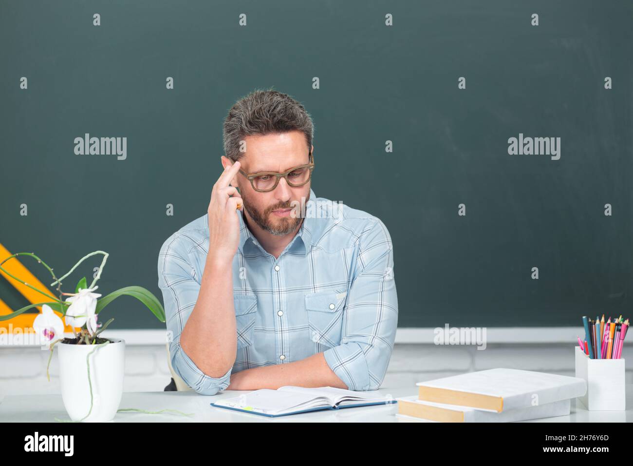 Portrait of thinking teacher or tutor professor working at table in ...