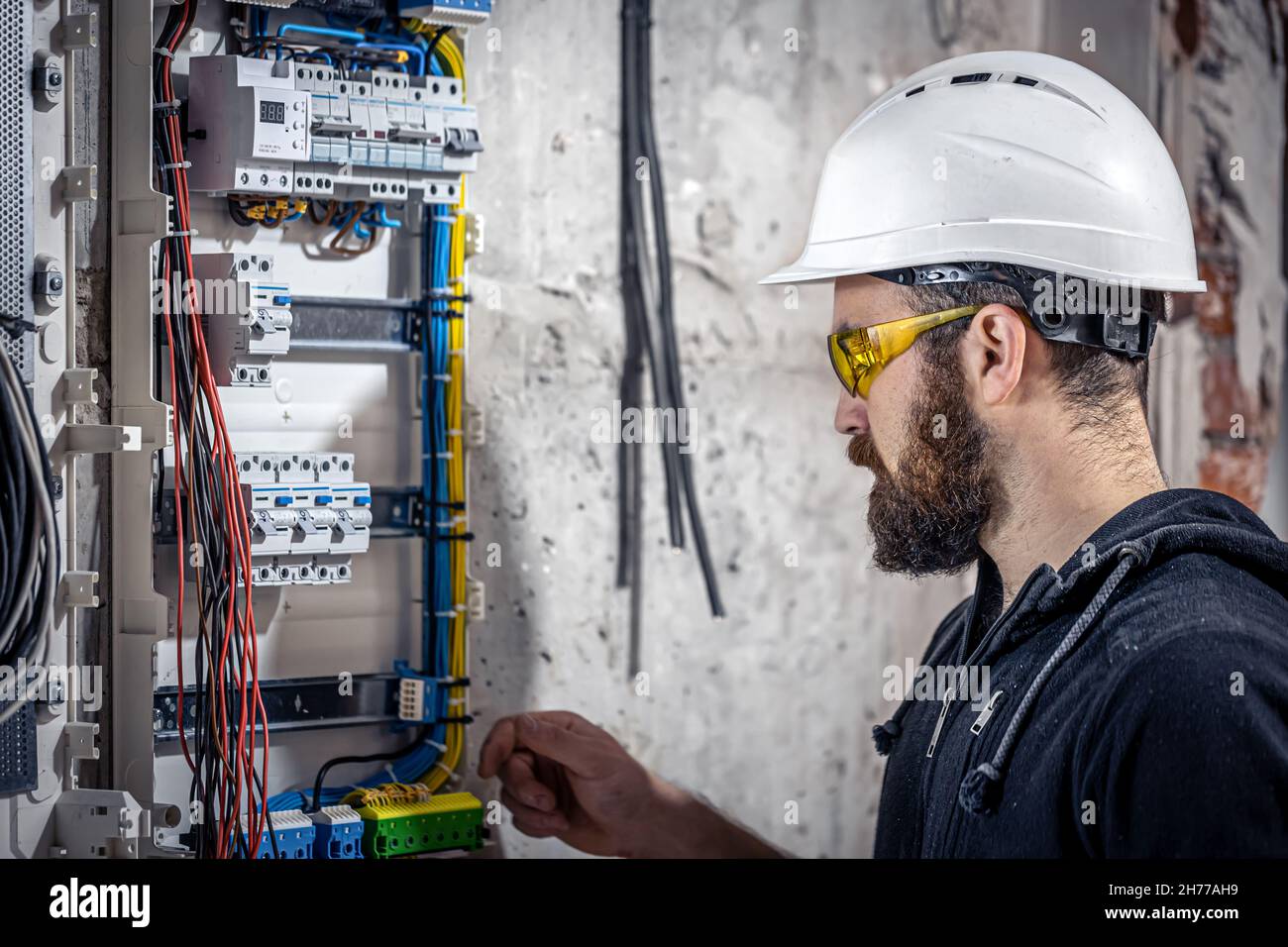 A male electrician works in a switchboard with an electrical connecting ...