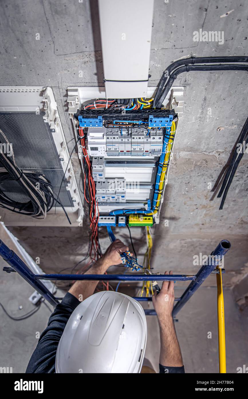 A male electrician works in a switchboard with an electrical connecting ...