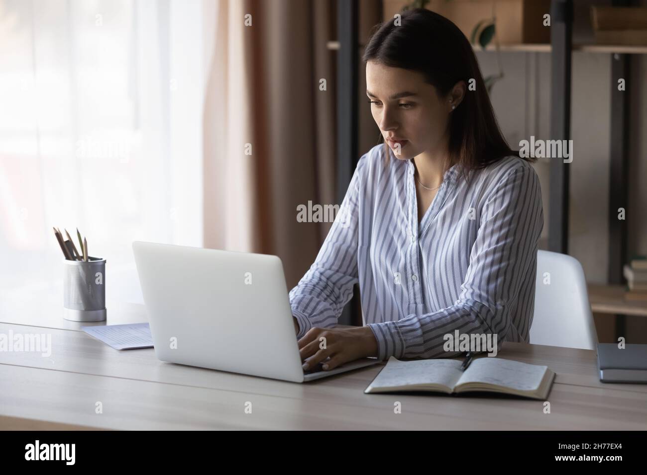 Focused smart young businesswoman working on computer at home office ...