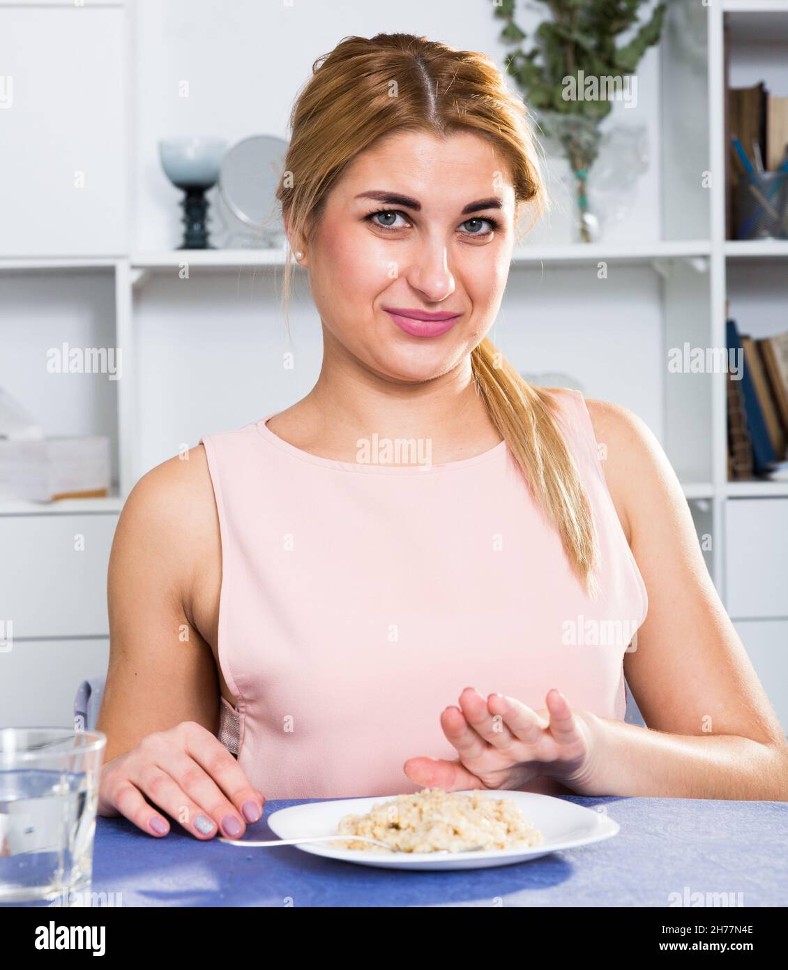 Young woman is eating tasteless oatmeal porridge and feeling disgust ...