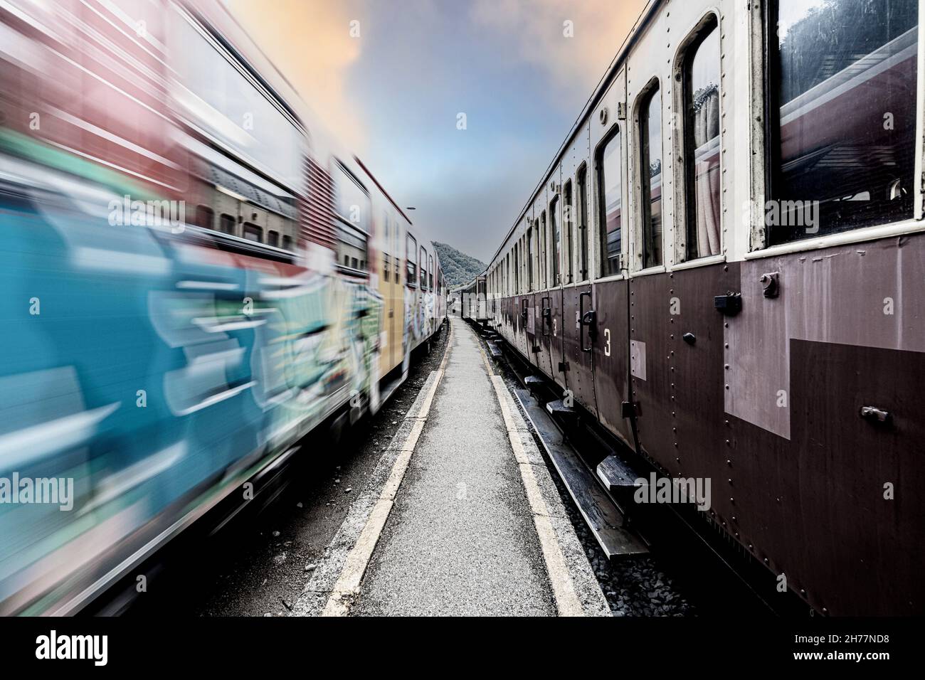 A scenery of trains at a station - one in movement and one stopped ...