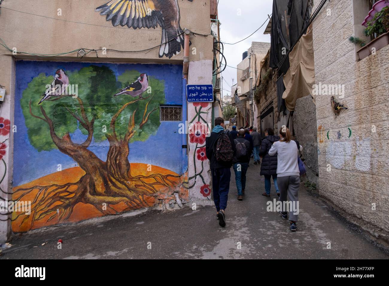 Tourists walk past a painted wall depicting goldfinches in Batn Al-Hawa ...