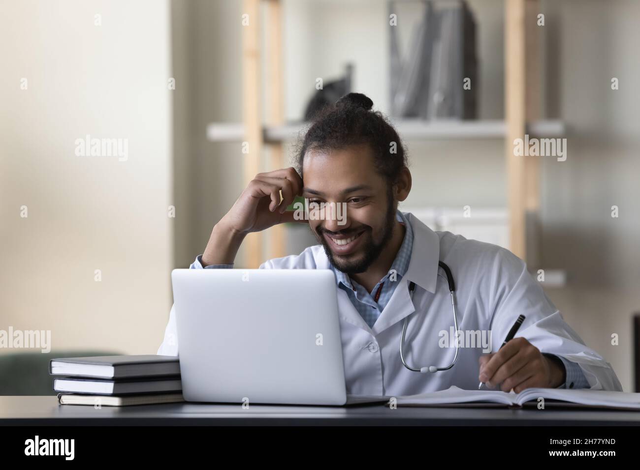 Smiling African American man doctor intern using laptop, taking notes ...