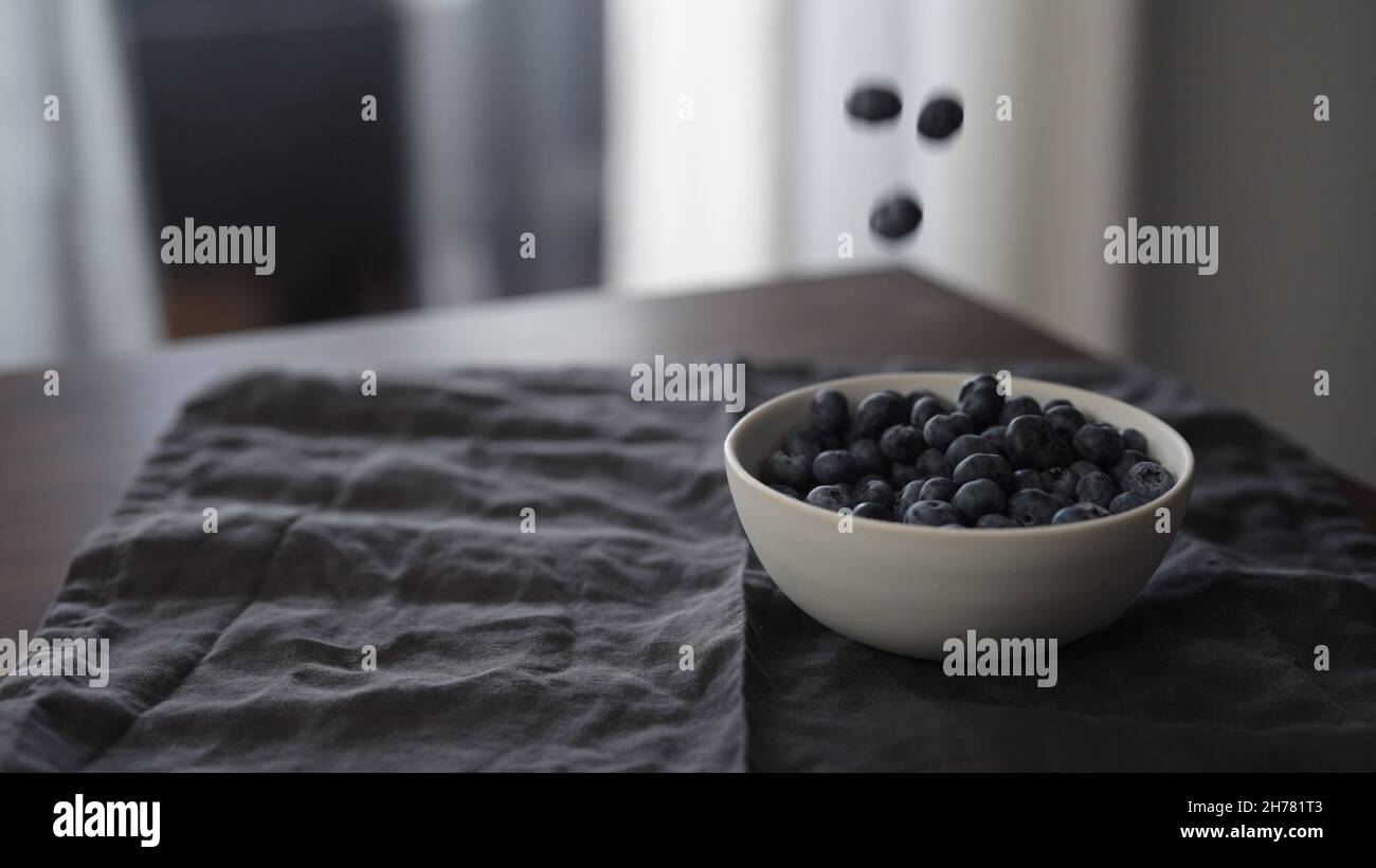 fresh blueberries fall into white bowl on table, wide photo Stock Photo ...