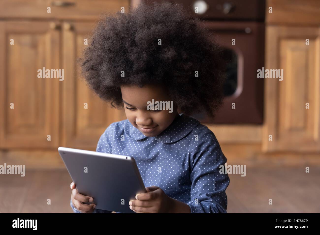 Happy small African ethnicity child girl playing on digital gadget ...