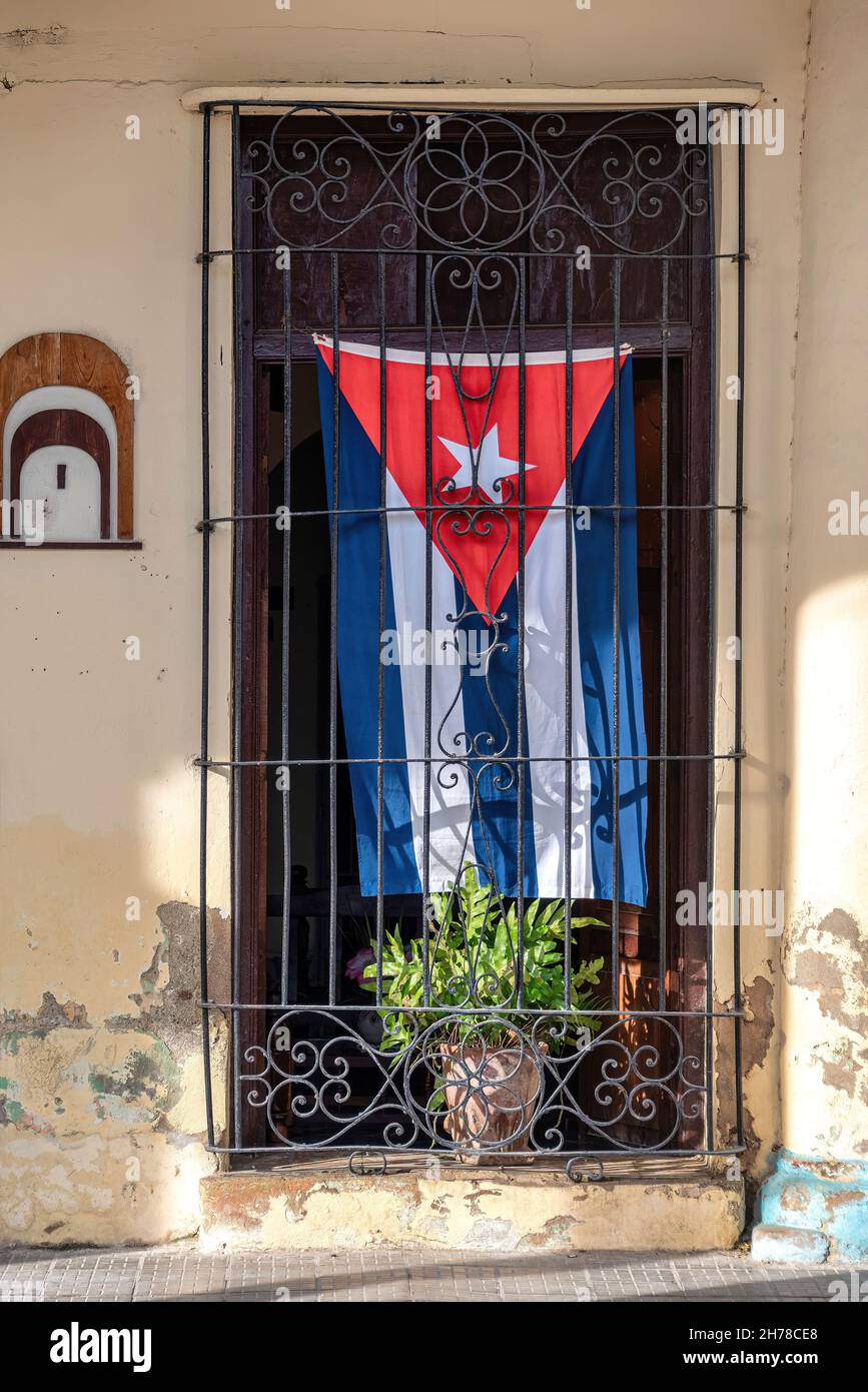 Cuban flag hanging on the metallic grid of colonial-style window in a ...