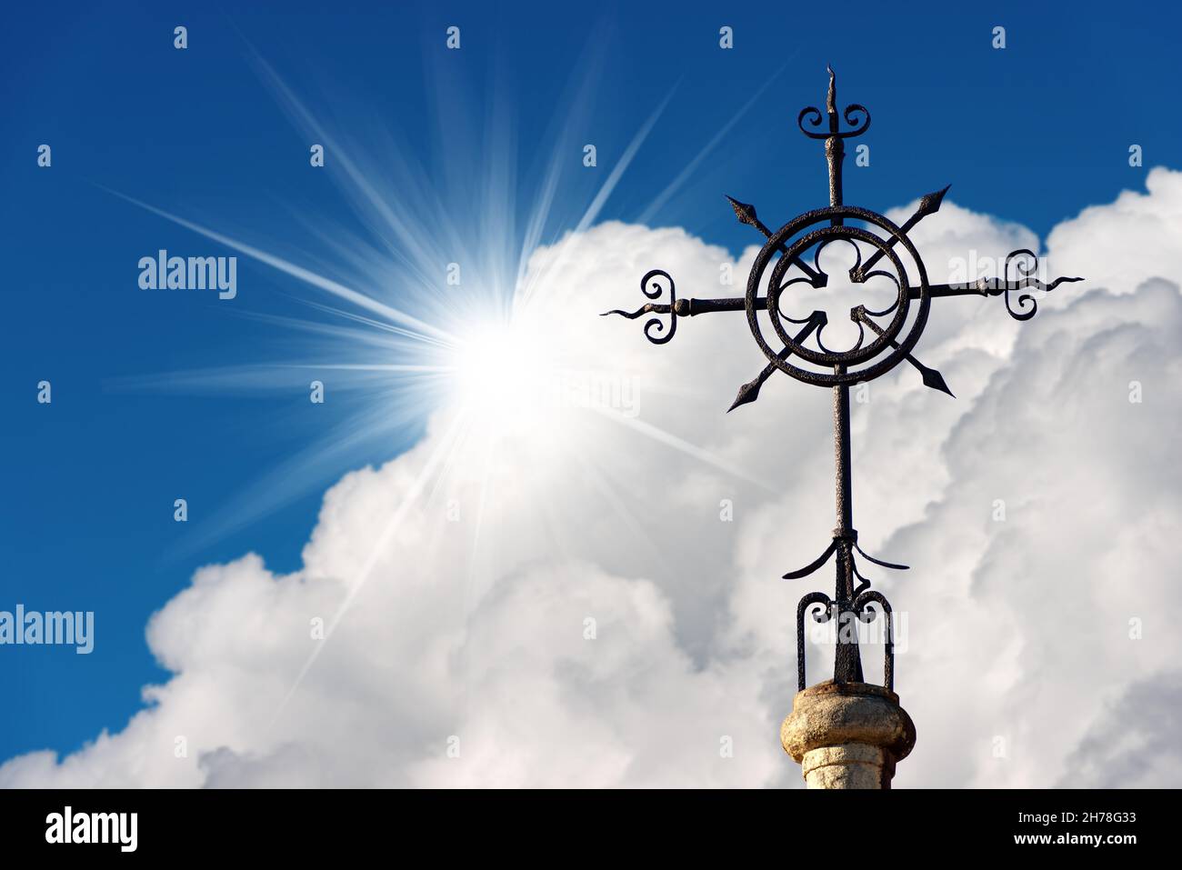 Wrought iron cross on a blue sky with clouds and sun rays, Christian ...