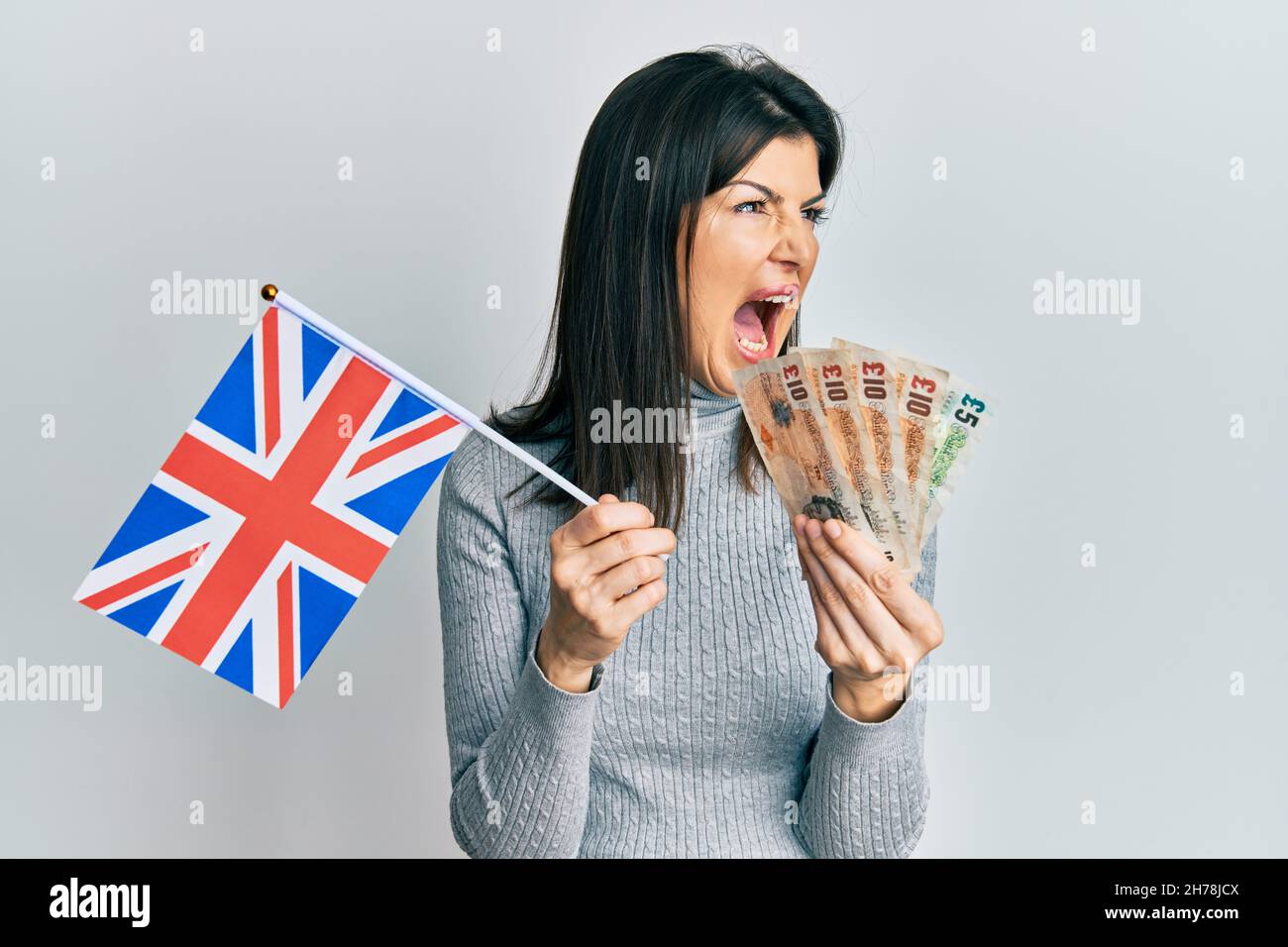Young hispanic woman holding united kingdom flag and pounds banknotes ...