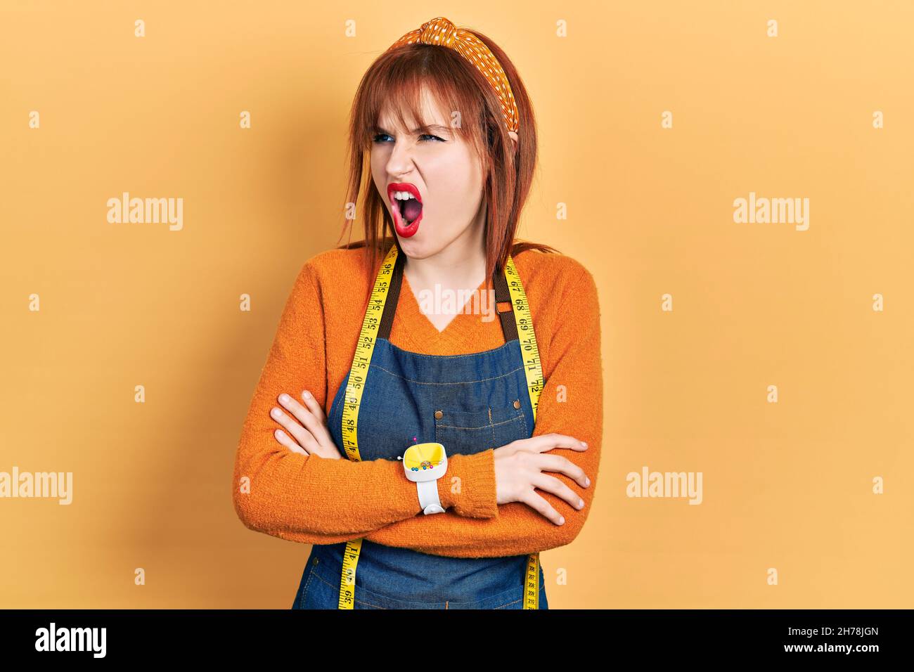 Redhead young woman dressmaker designer wearing atelier apron angry and ...