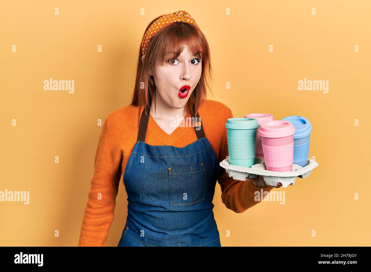 Redhead young woman wearing waitress apron holding take away cups of ...