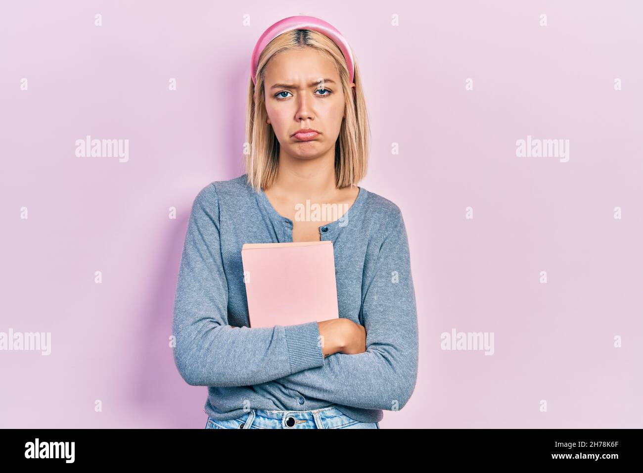 Beautiful blonde woman holding book depressed and worry for distress ...