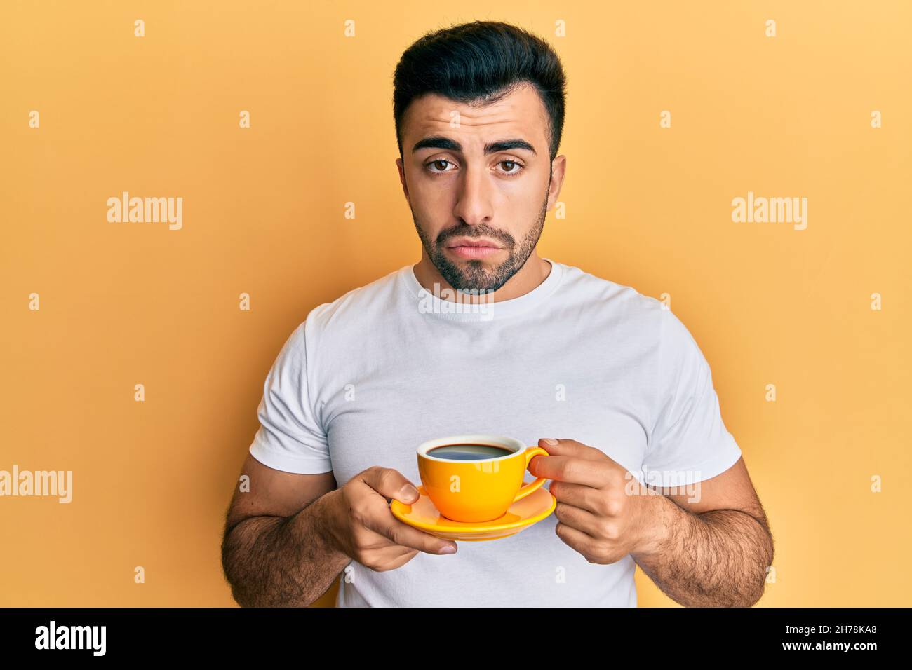 Young hispanic man drinking a cup of coffee depressed and worry for ...