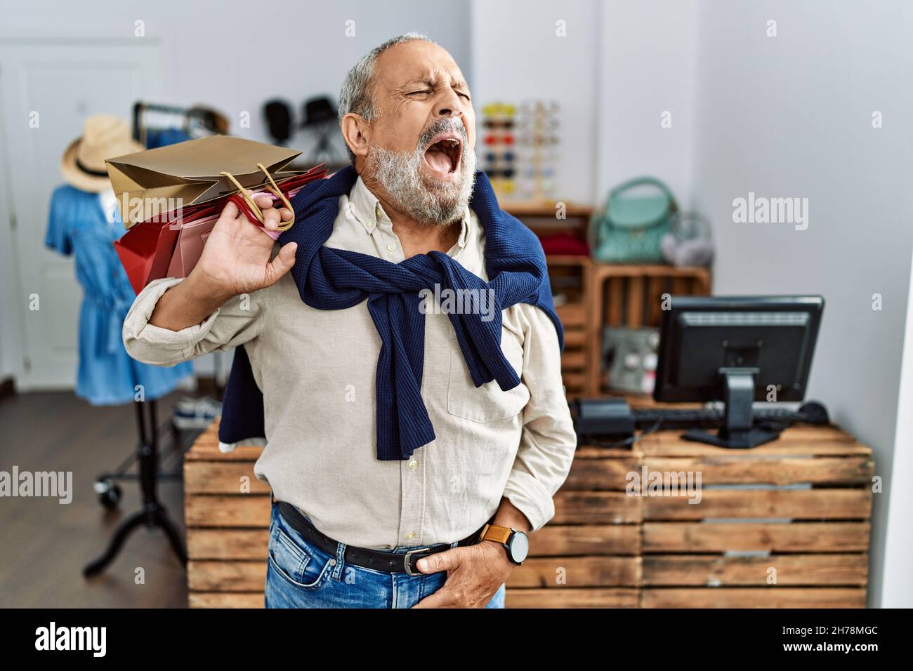 Handsome senior man holding shopping bags at boutique shop angry and ...