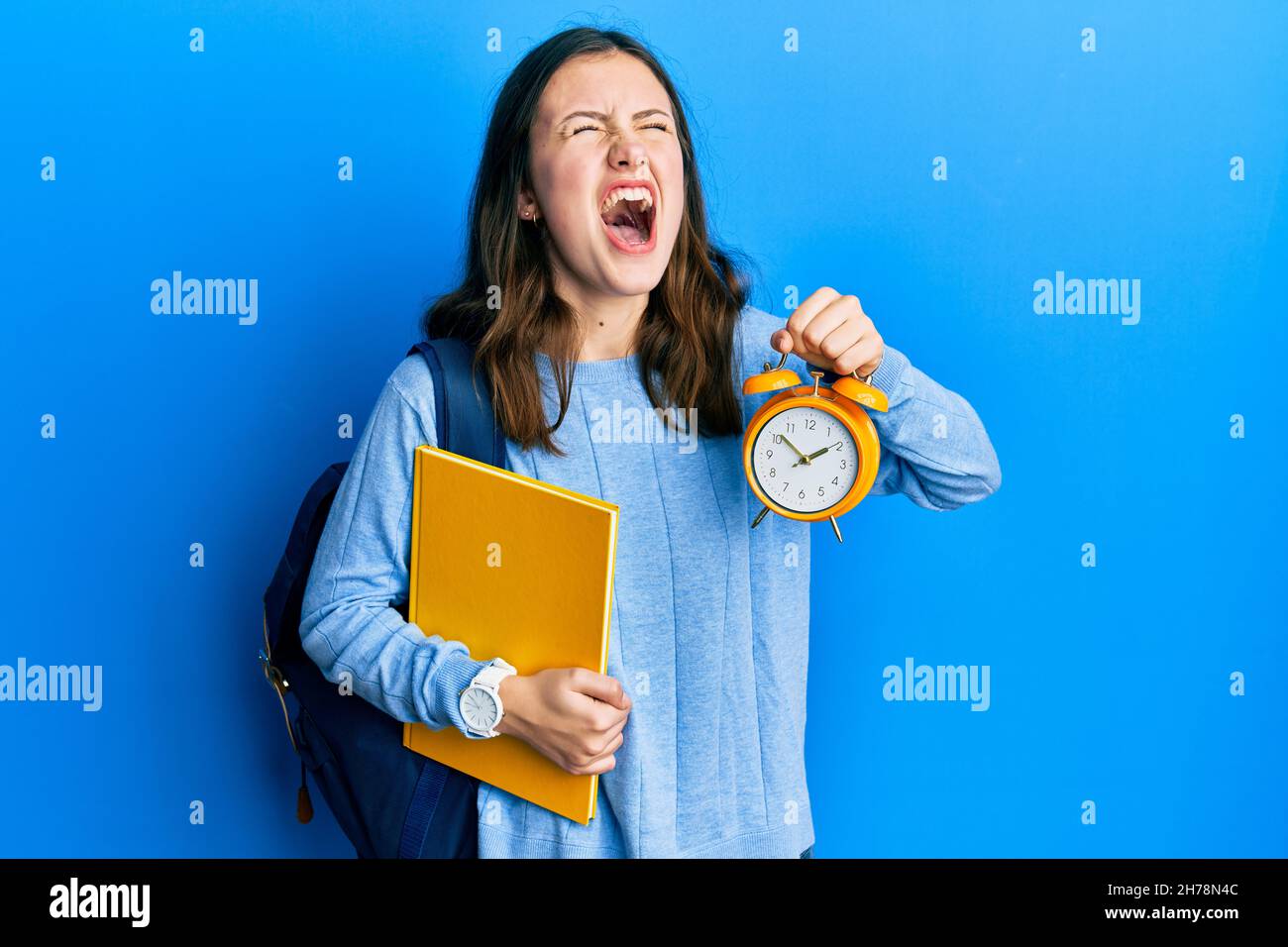 Young brunette student woman holding alarm clock angry and mad ...