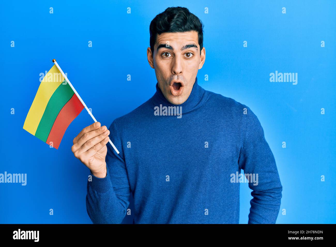 Handsome hispanic man holding lithuania flag scared and amazed with ...