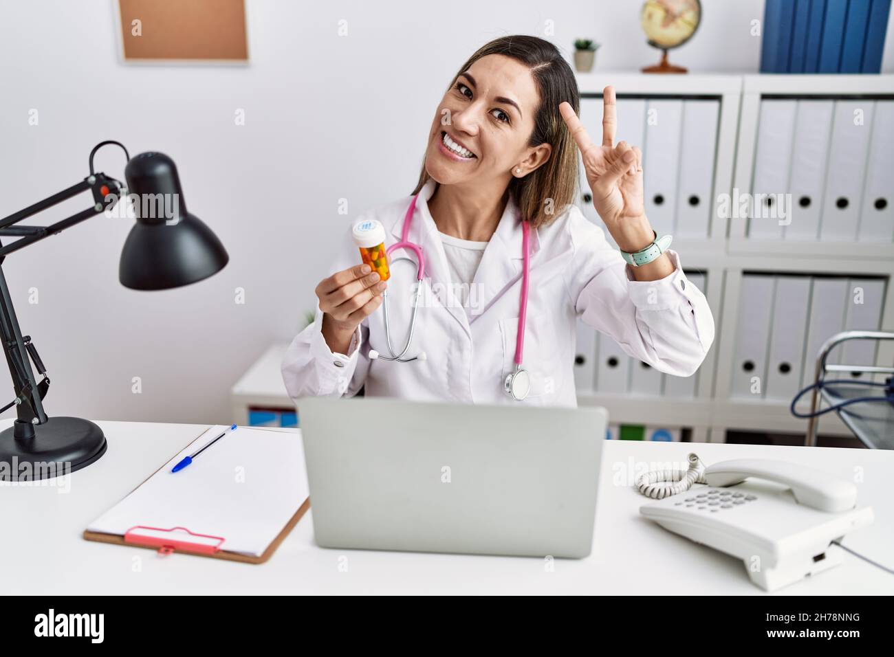 Young hispanic woman wearing doctor uniform holding pills at the clinic ...