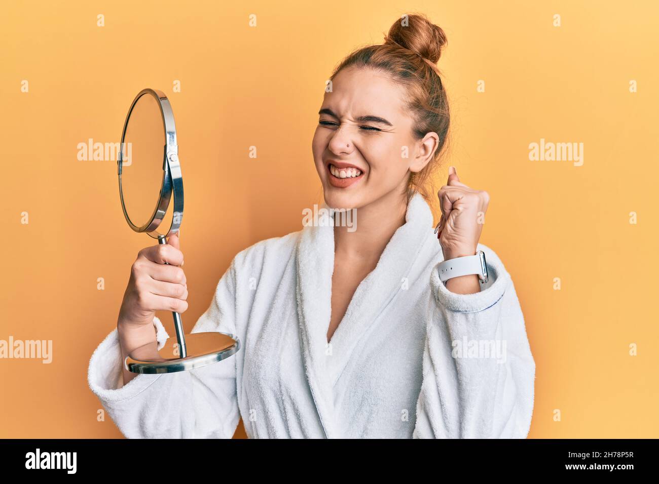 Young blonde woman wearing robe holding mirror screaming proud ...