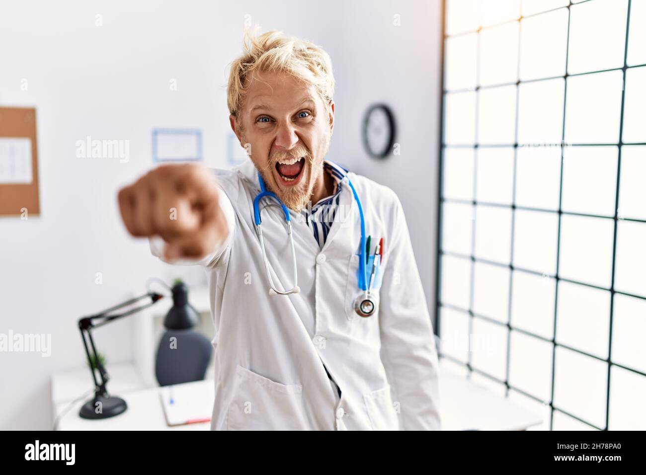 Young blond man wearing doctor uniform and stethoscope at clinic ...