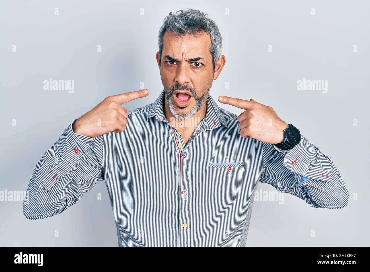 Handsome middle age man with grey hair pointing mouth with fingers in ...