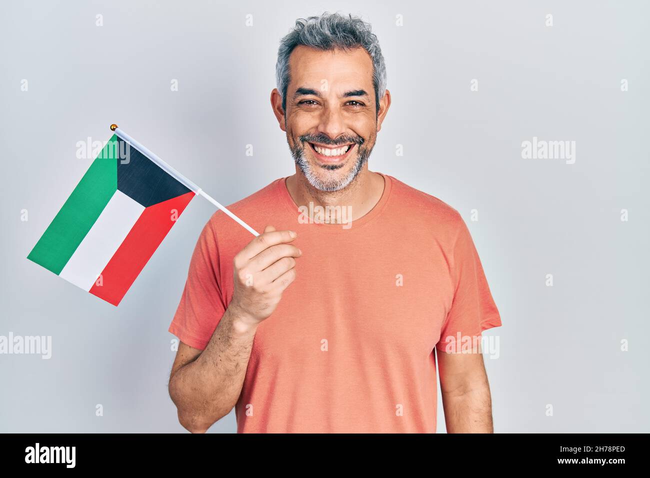 Handsome middle age man with grey hair holding kuwait flag looking ...