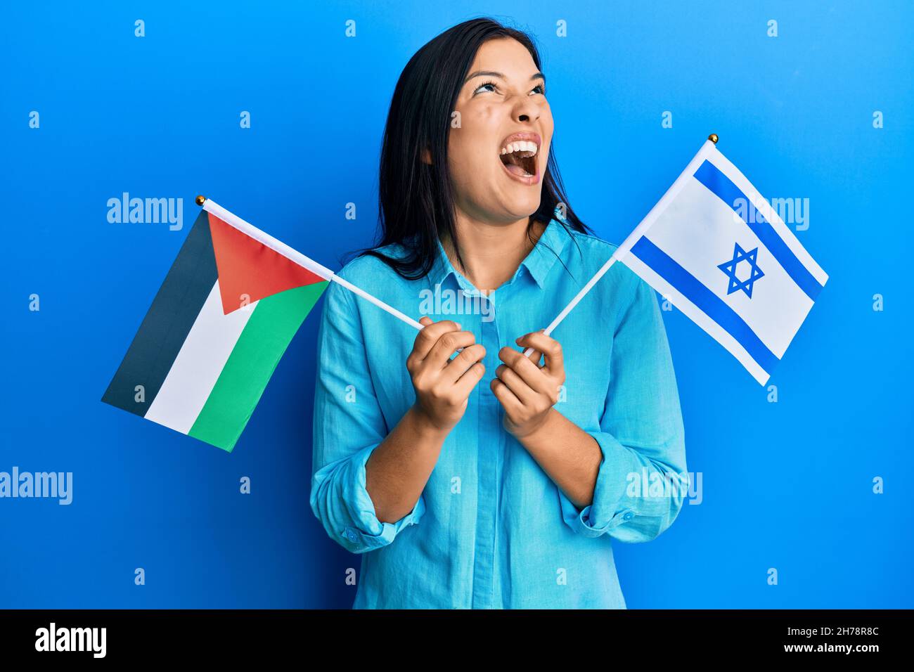 Young latin woman holding palestine and israel flags angry and mad ...