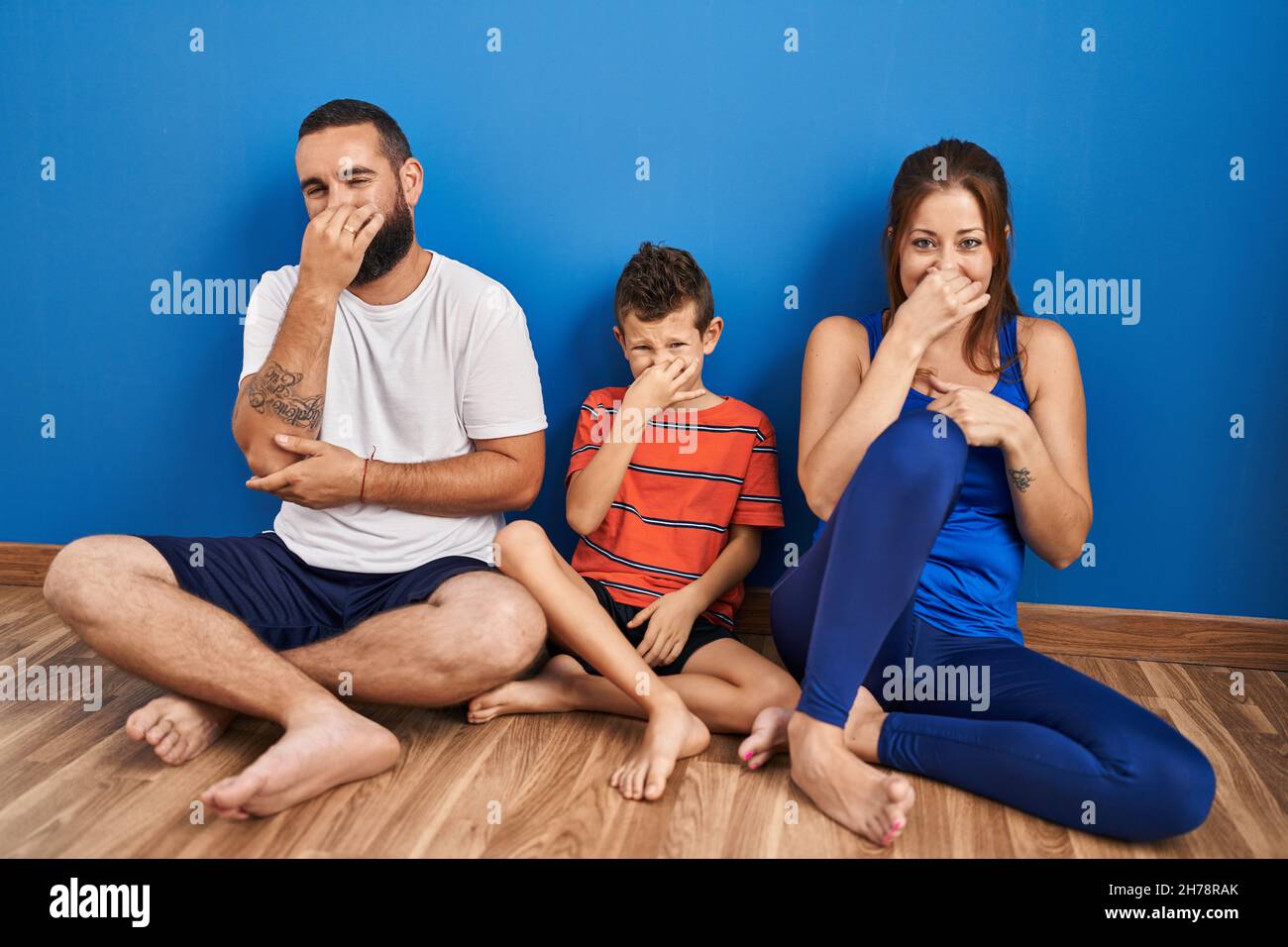 Family of three sitting on the floor at home smelling something stinky ...