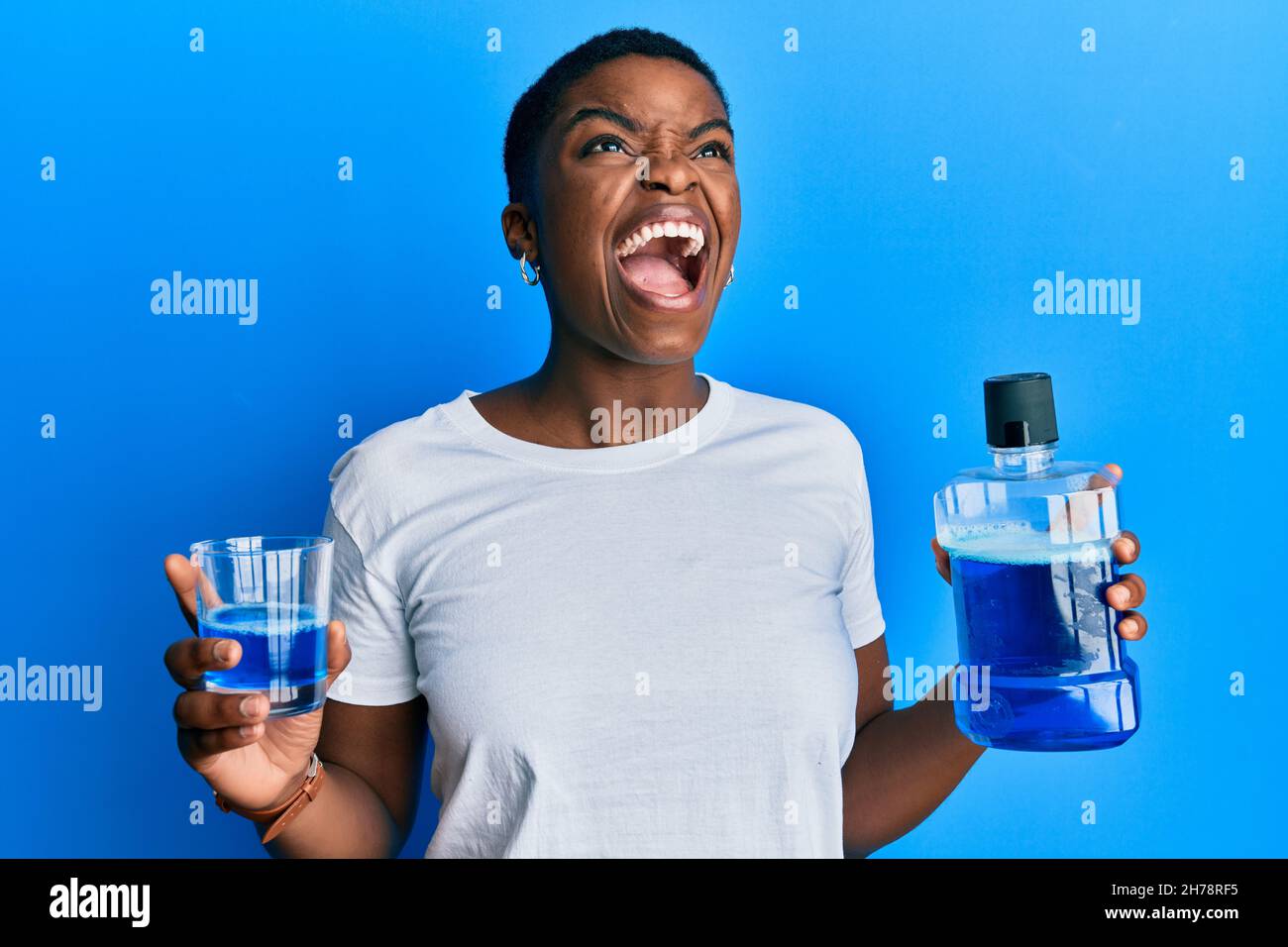 Young african american woman holding mouthwash for fresh breath angry ...