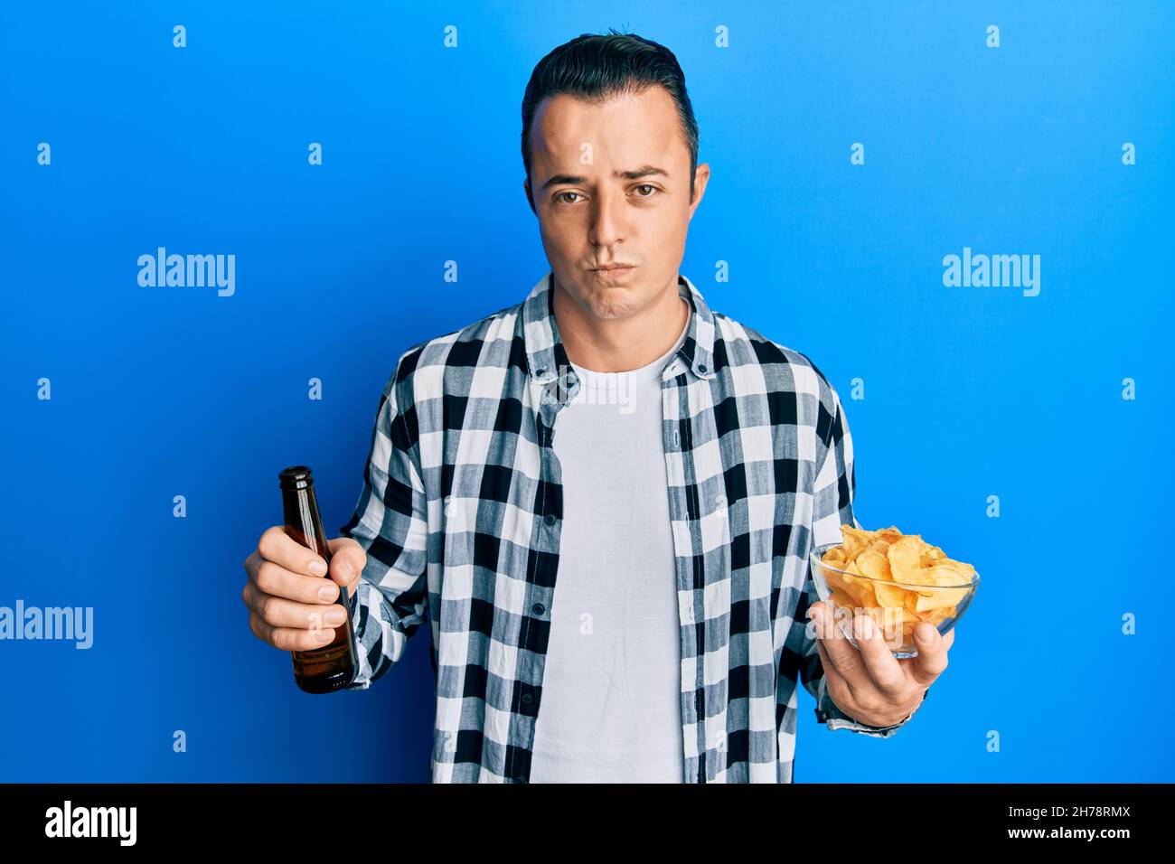 Handsome young man drinking a pint of beer holding chips depressed and ...