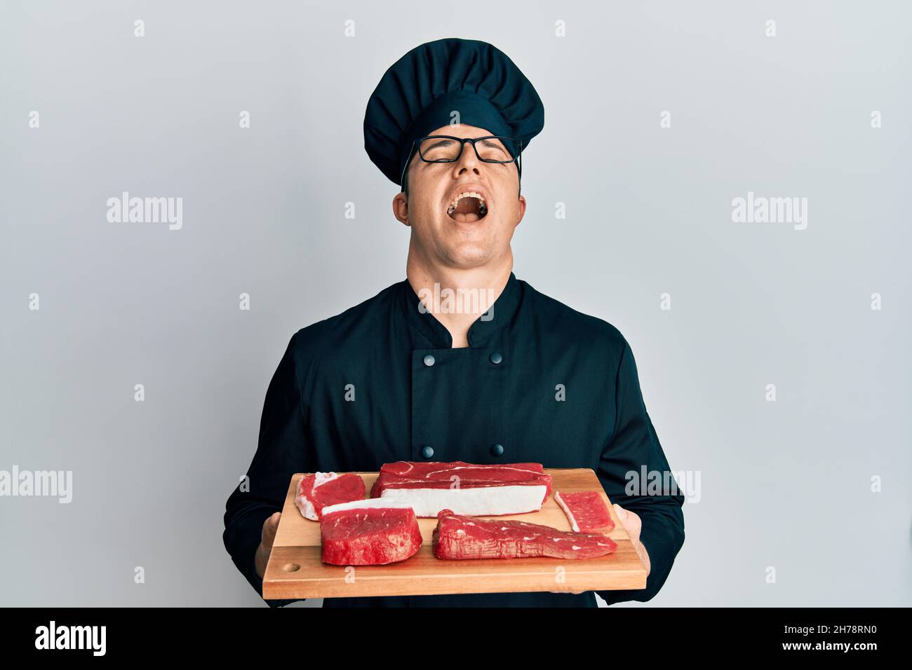 Handsome young man wearing chef uniform holding board with raw meat ...